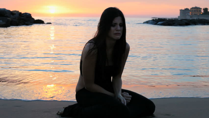 Worried Sad Girl In Long Dress Sitting On The Beach At Sunset. Slow ...